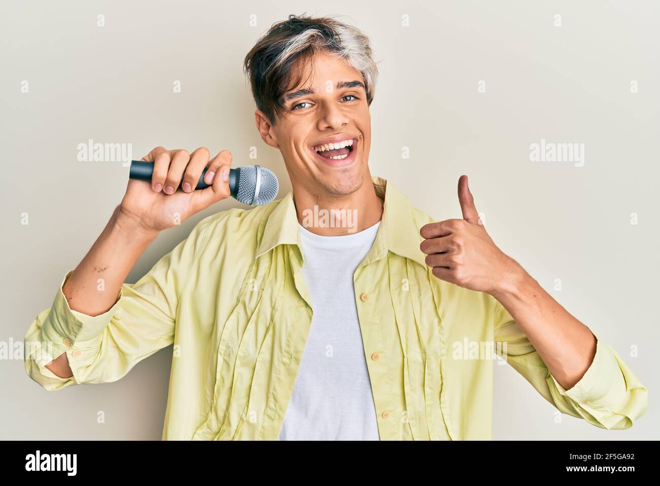 Young hispanic man singing song using microphone smiling happy and ...