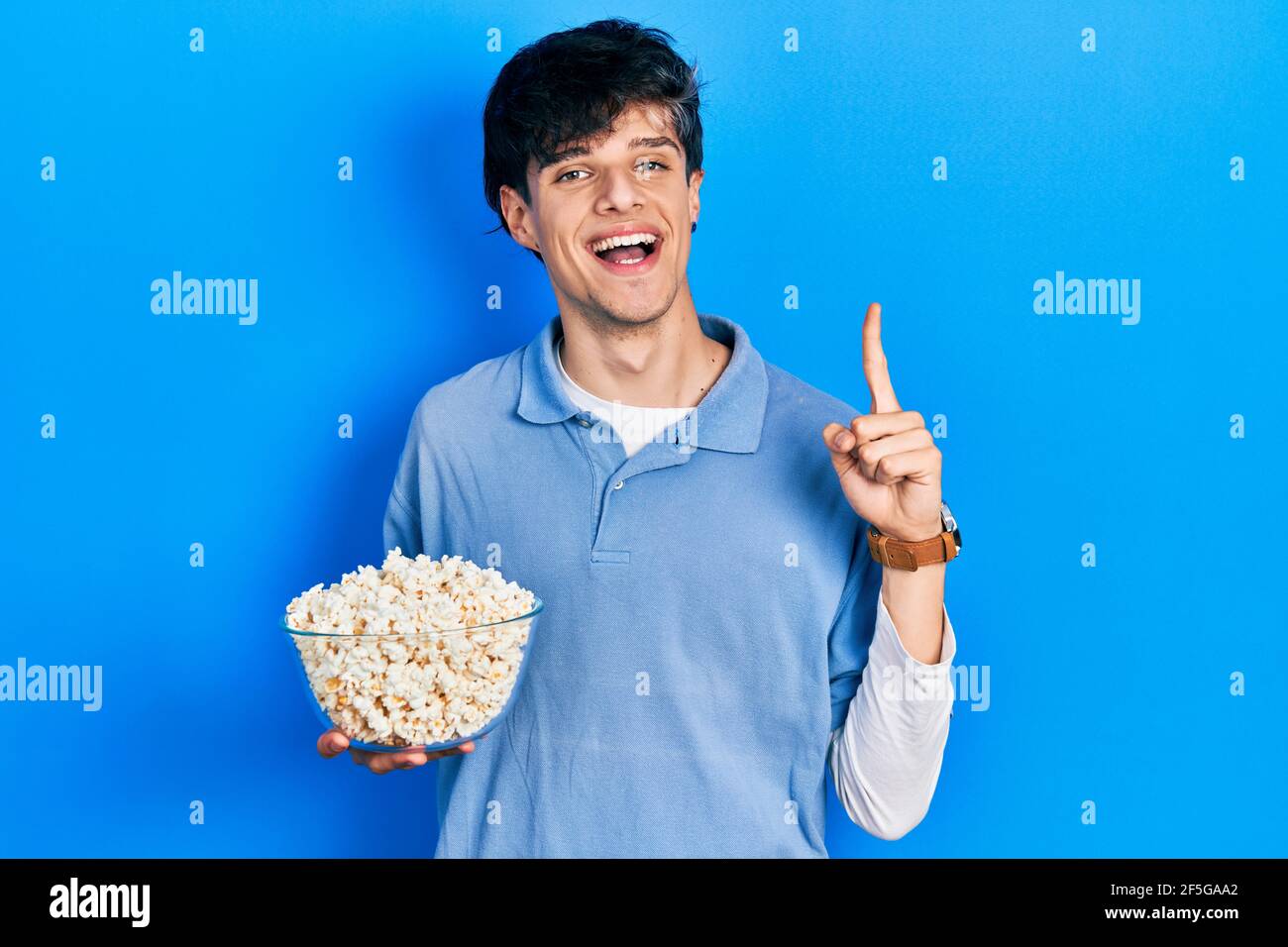 Handsome hipster young man eating popcorn smiling with an idea or ...