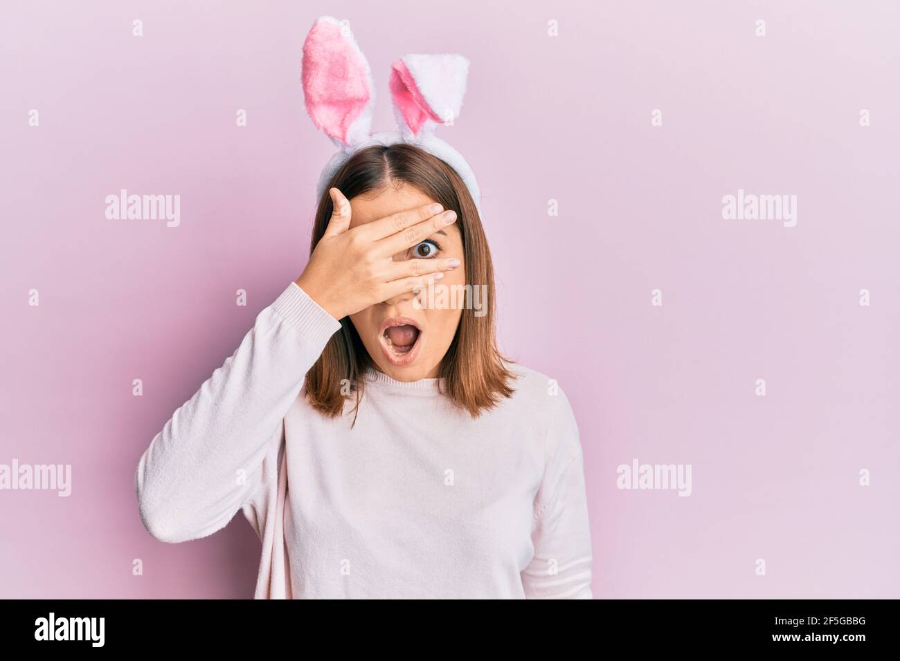 Young beautiful woman wearing cute easter bunny ears peeking in shock ...