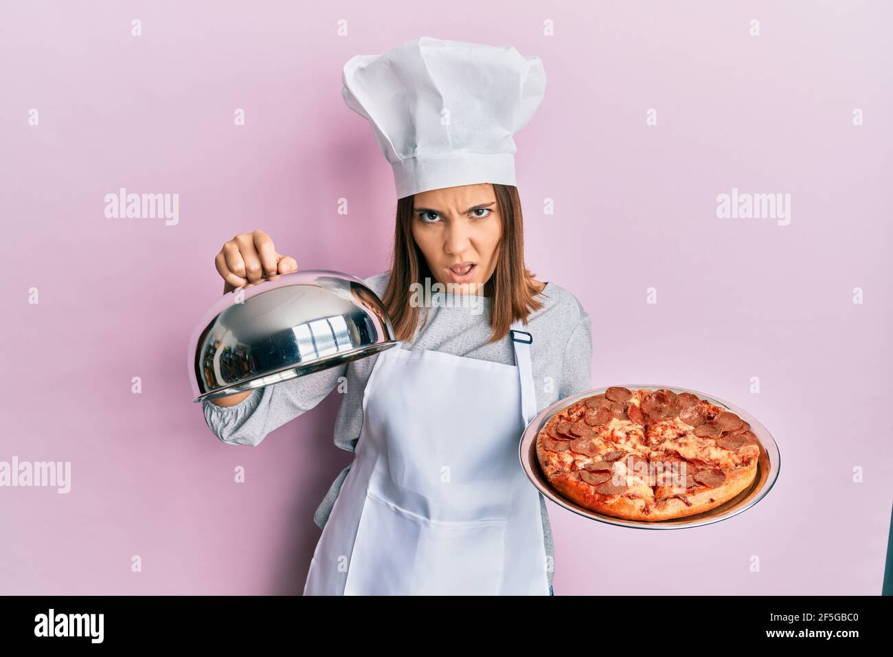 Young beautiful woman professional cook holding italian pizza in shock ...