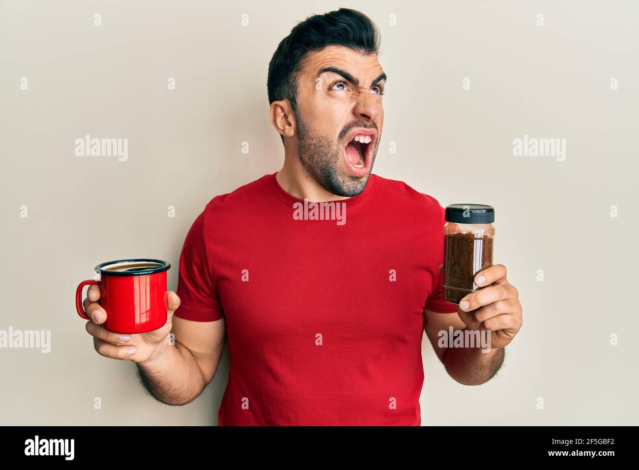 Young hispanic man holding cup of soluble coffee angry and mad ...
