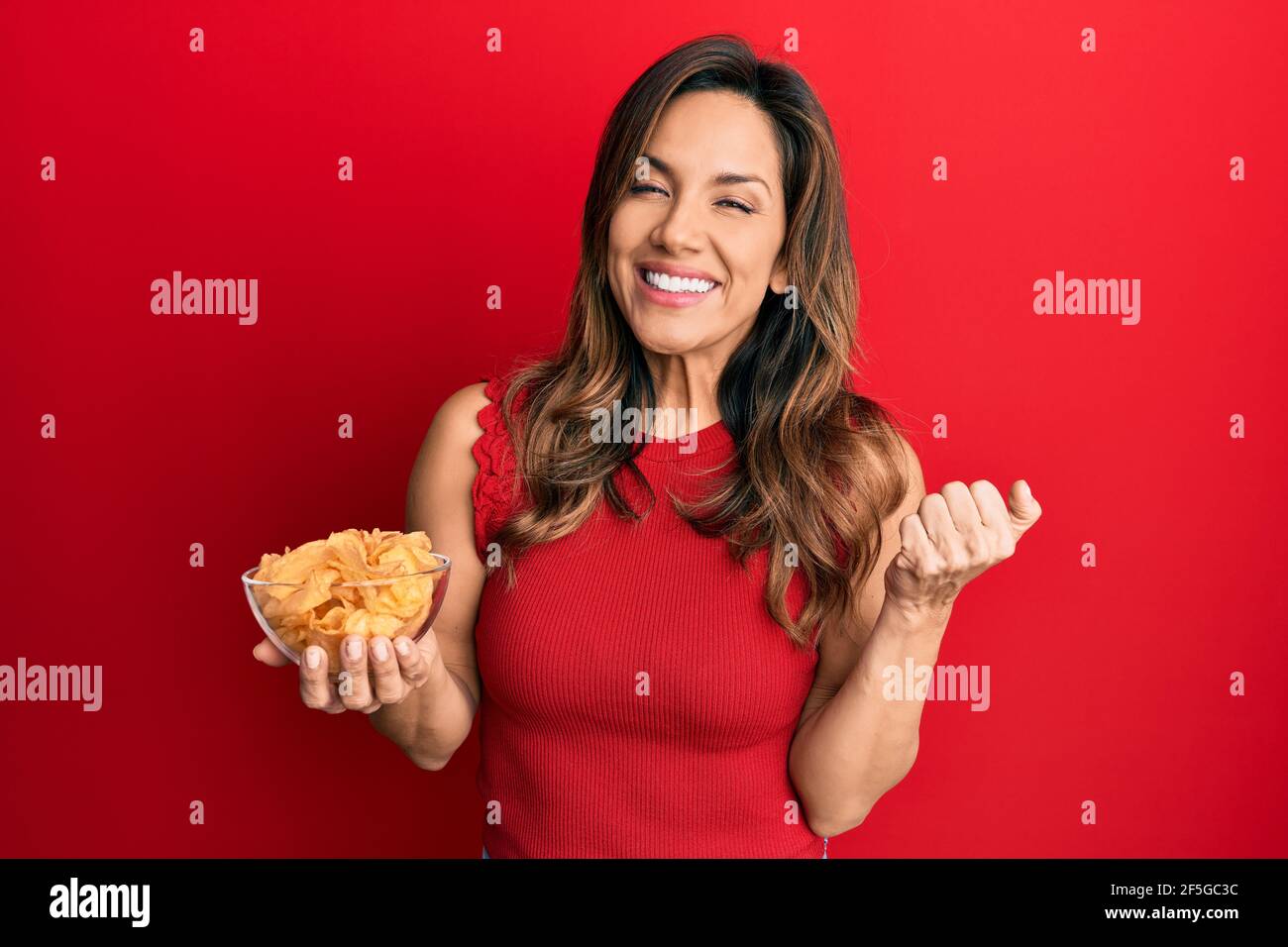 Young latin woman holding potato chip screaming proud, celebrating ...