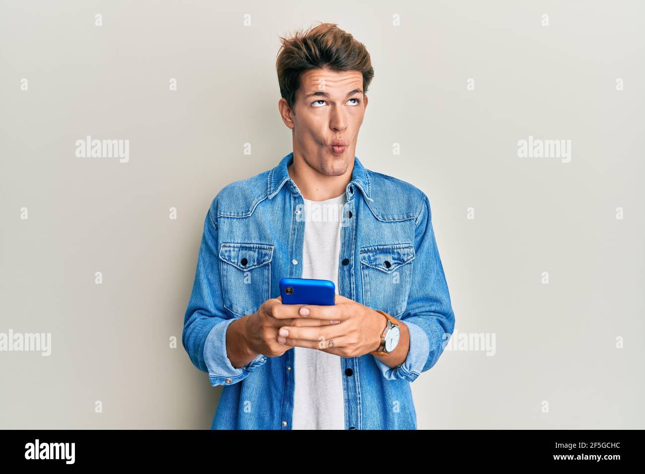 Handsome caucasian man using smartphone making fish face with mouth and ...