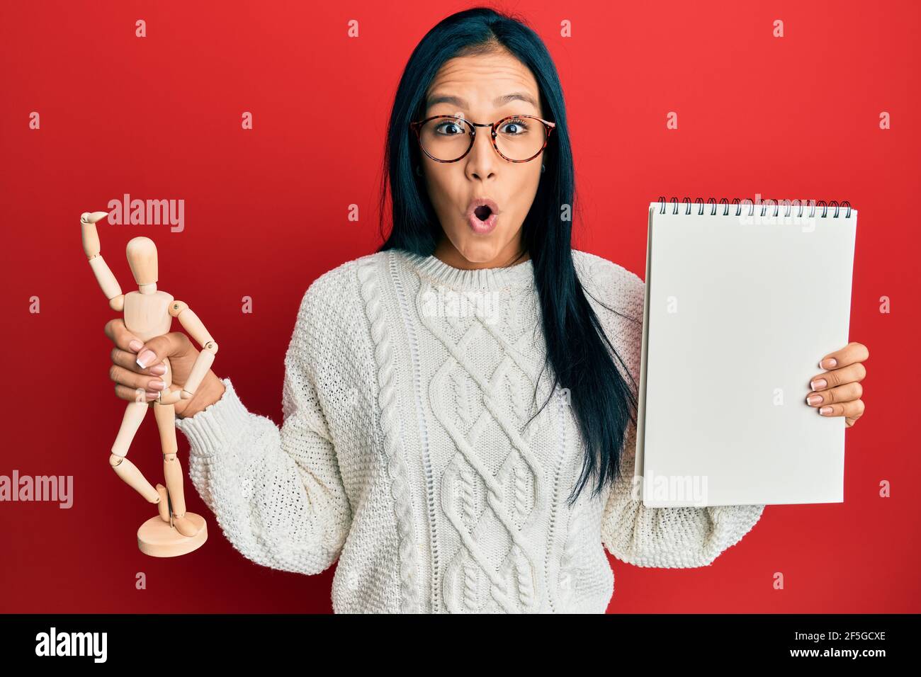 Beautiful hispanic woman holding small wooden manikin and notebook ...