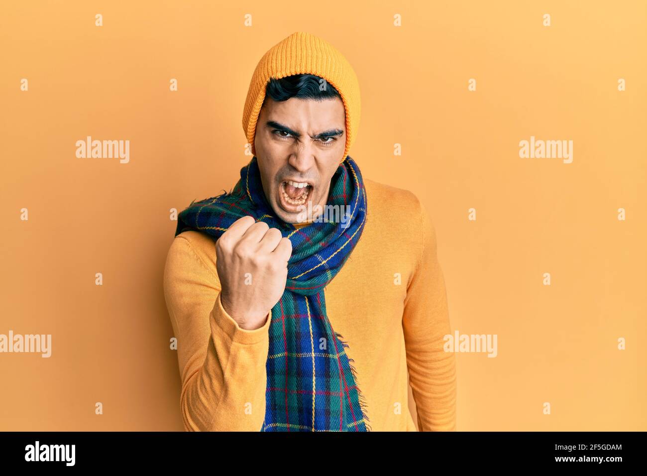 Handsome hispanic man wearing wool hat and winter scarf angry and mad ...