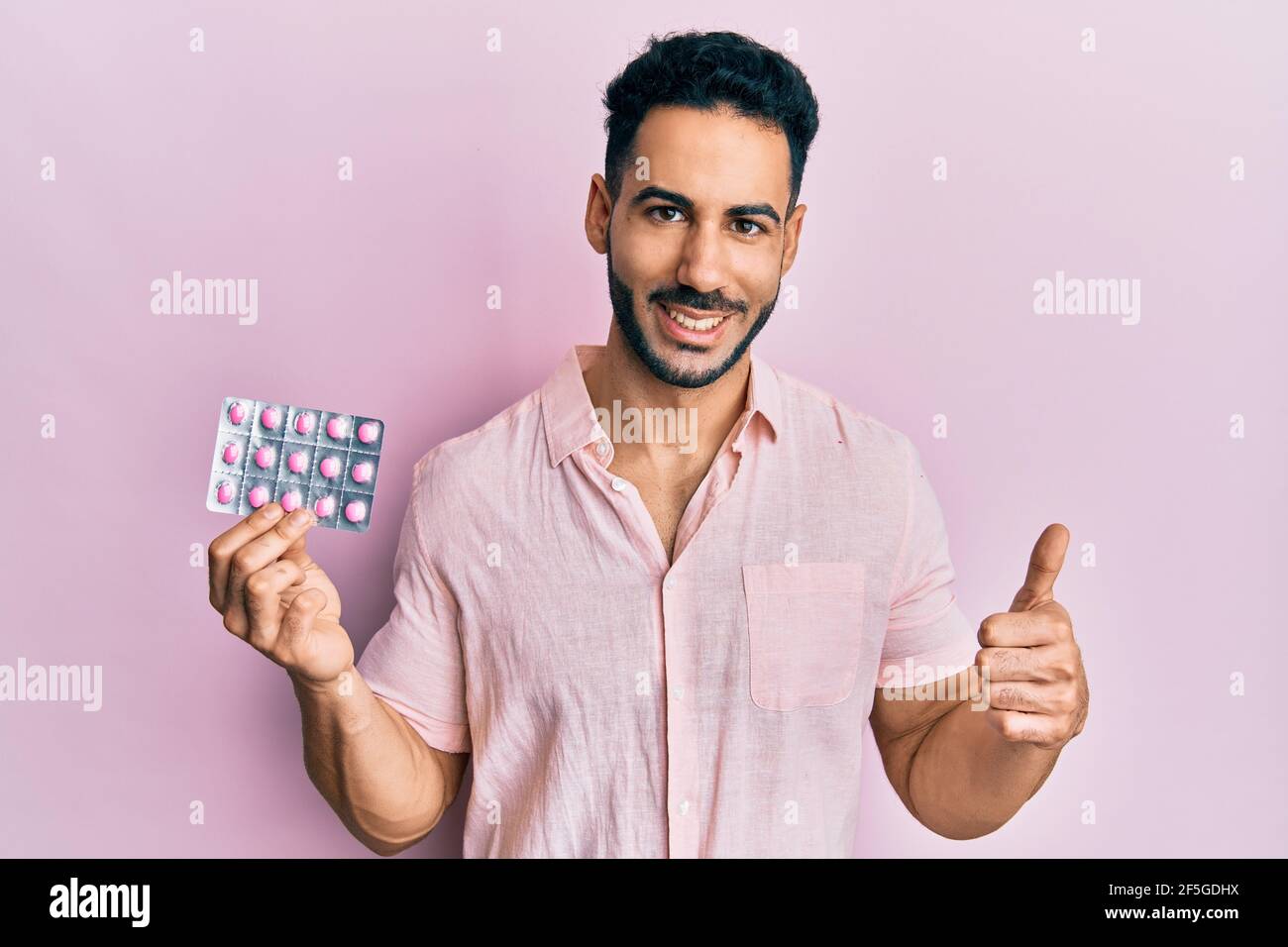 Young hispanic man holding pills smiling happy and positive, thumb up ...