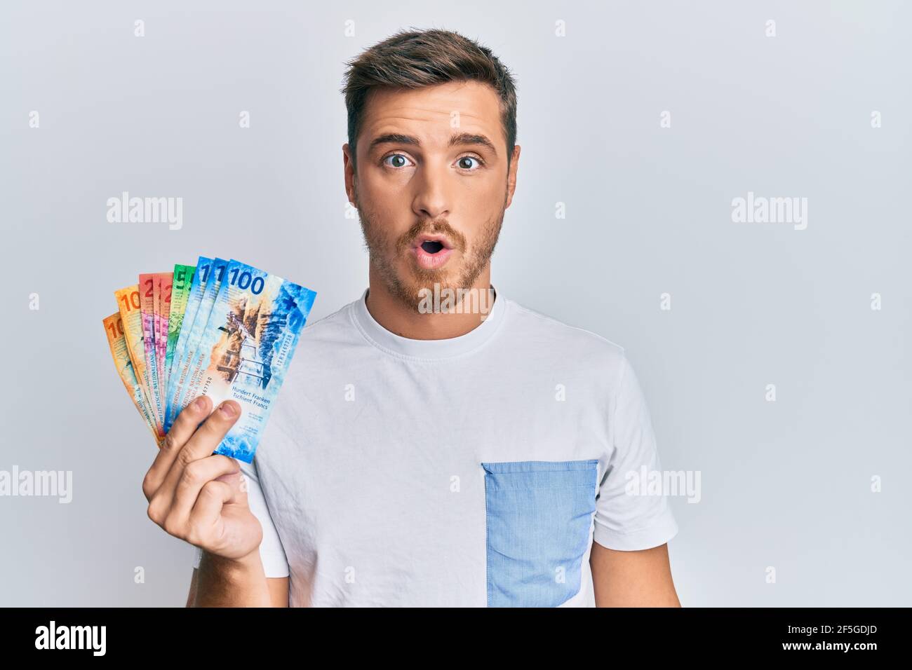 Handsome caucasian man holding swiss franc banknotes scared and amazed ...