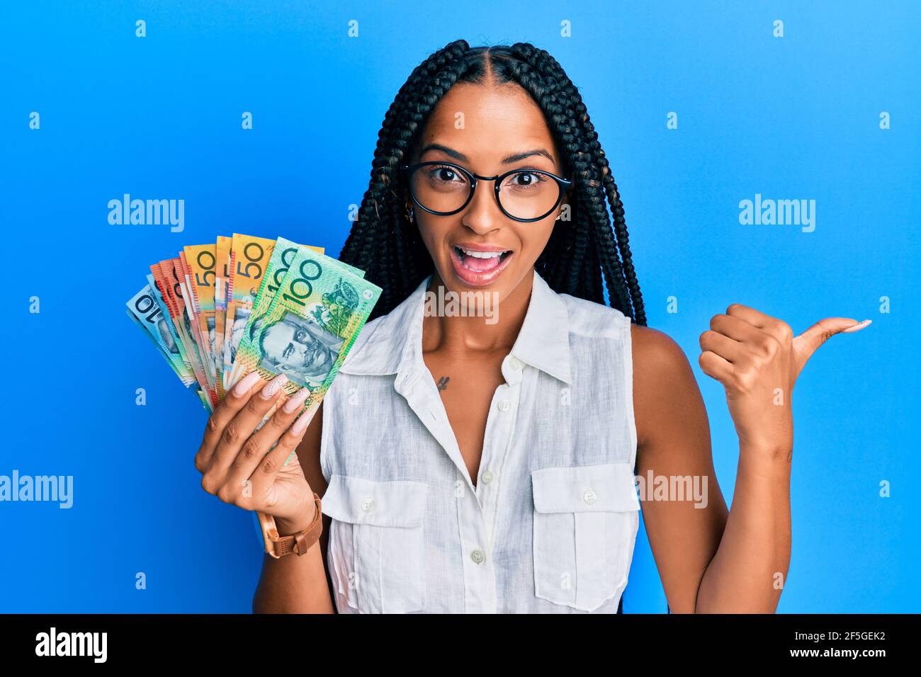 Beautiful hispanic woman holding australian dollars pointing thumb up ...