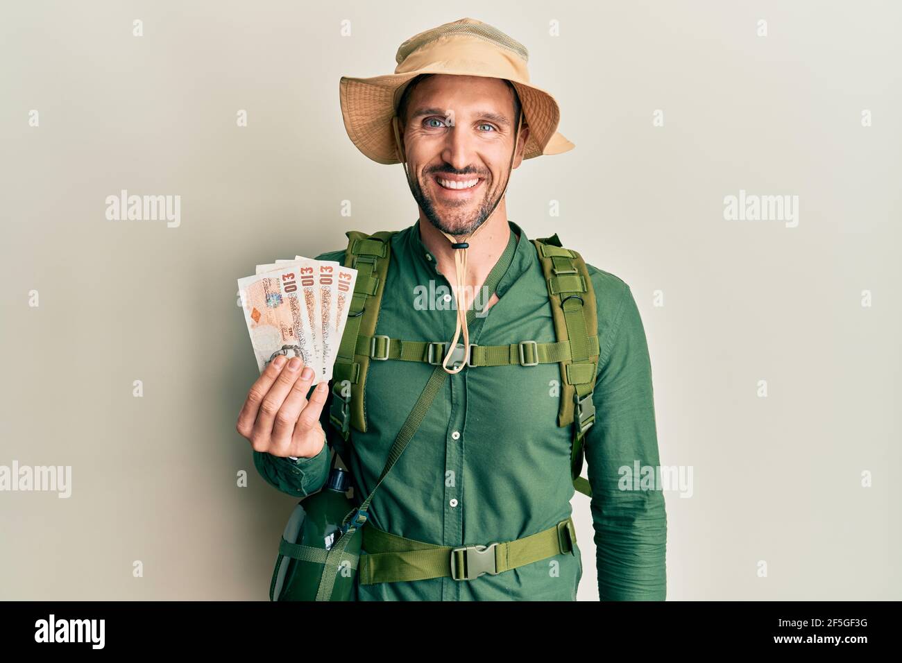 Handsome man with beard wearing explorer hat holding 10 pounds looking ...