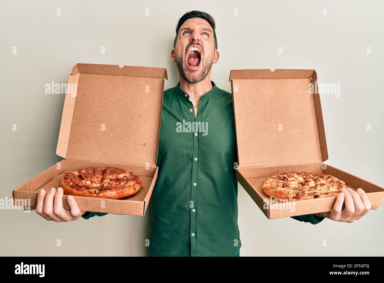 Handsome man with beard holding two italian pizzas angry and mad ...