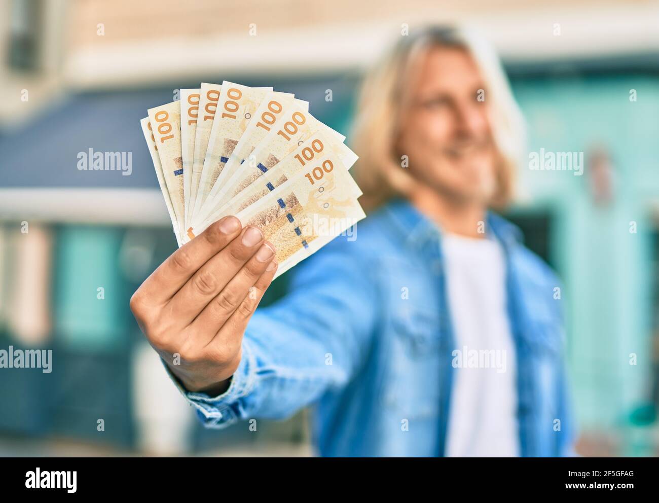 Young blond scandinavian man smiling happy holding danmark 100 kroner ...