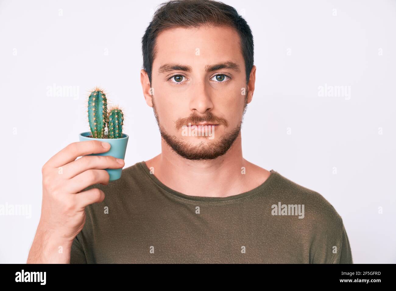 Young handsome man holding small cactus pot thinking attitude and sober ...