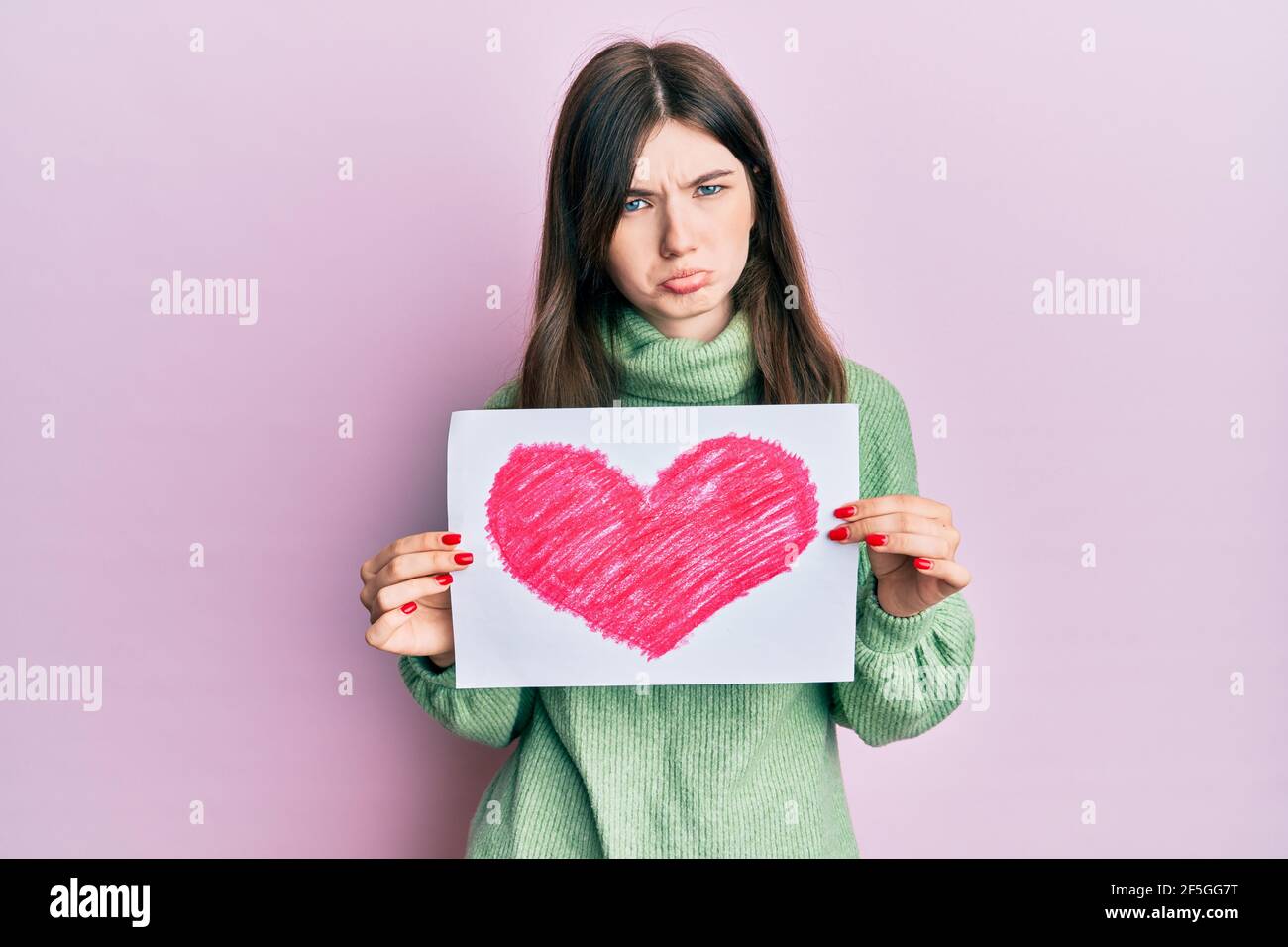 Young beautiful caucasian girl holding heart draw depressed and worry ...