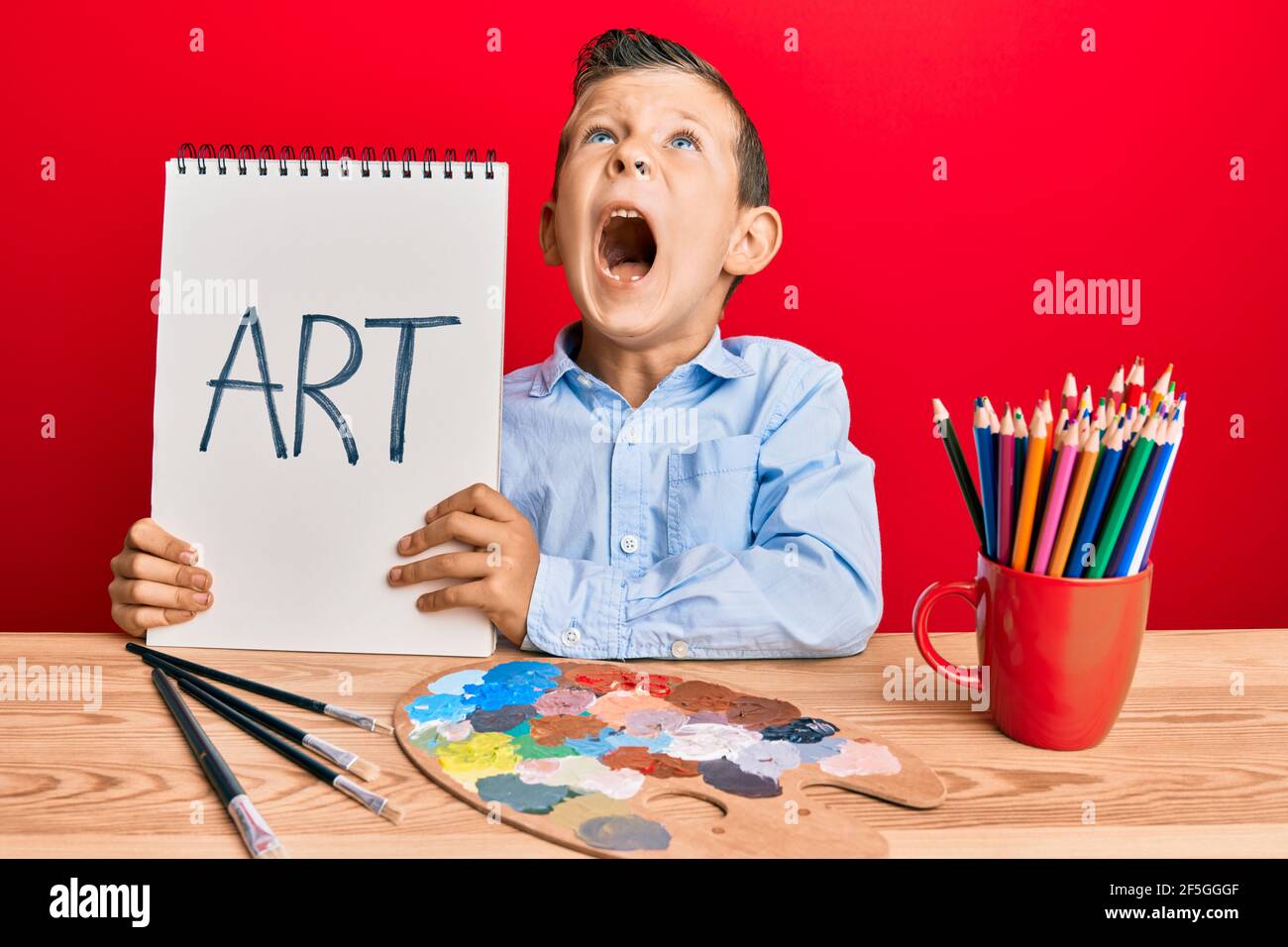 Adorable caucasian kid painter sitting at art studio holding art word ...