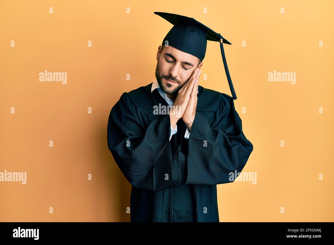 Young hispanic man wearing graduation cap and ceremony robe sleeping ...