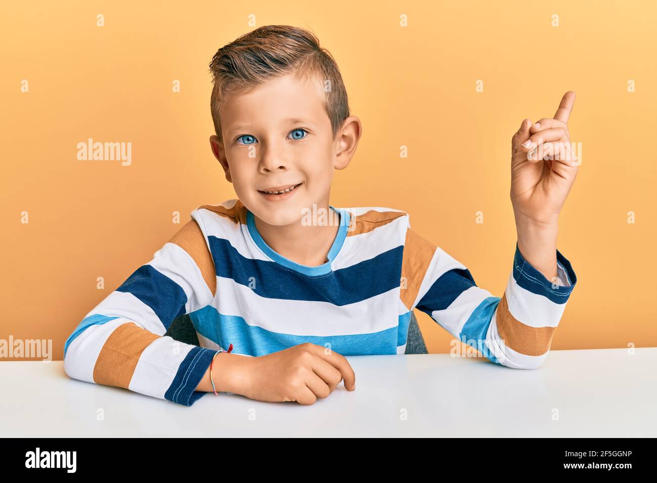 Adorable caucasian kid wearing casual clothes sitting on the table with ...