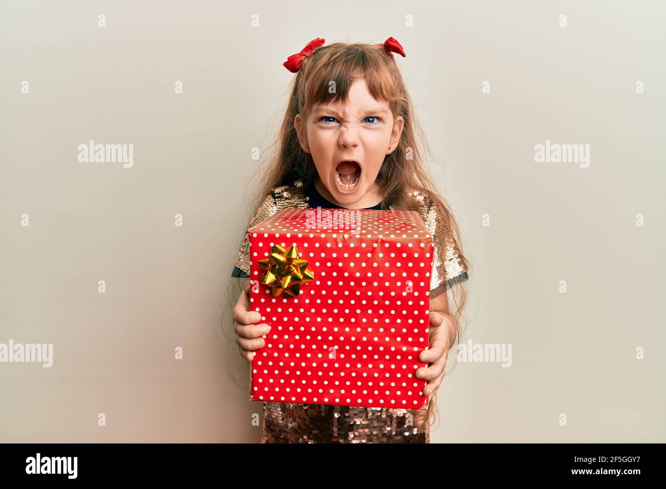Little caucasian girl kid holding red gift angry and mad screaming ...