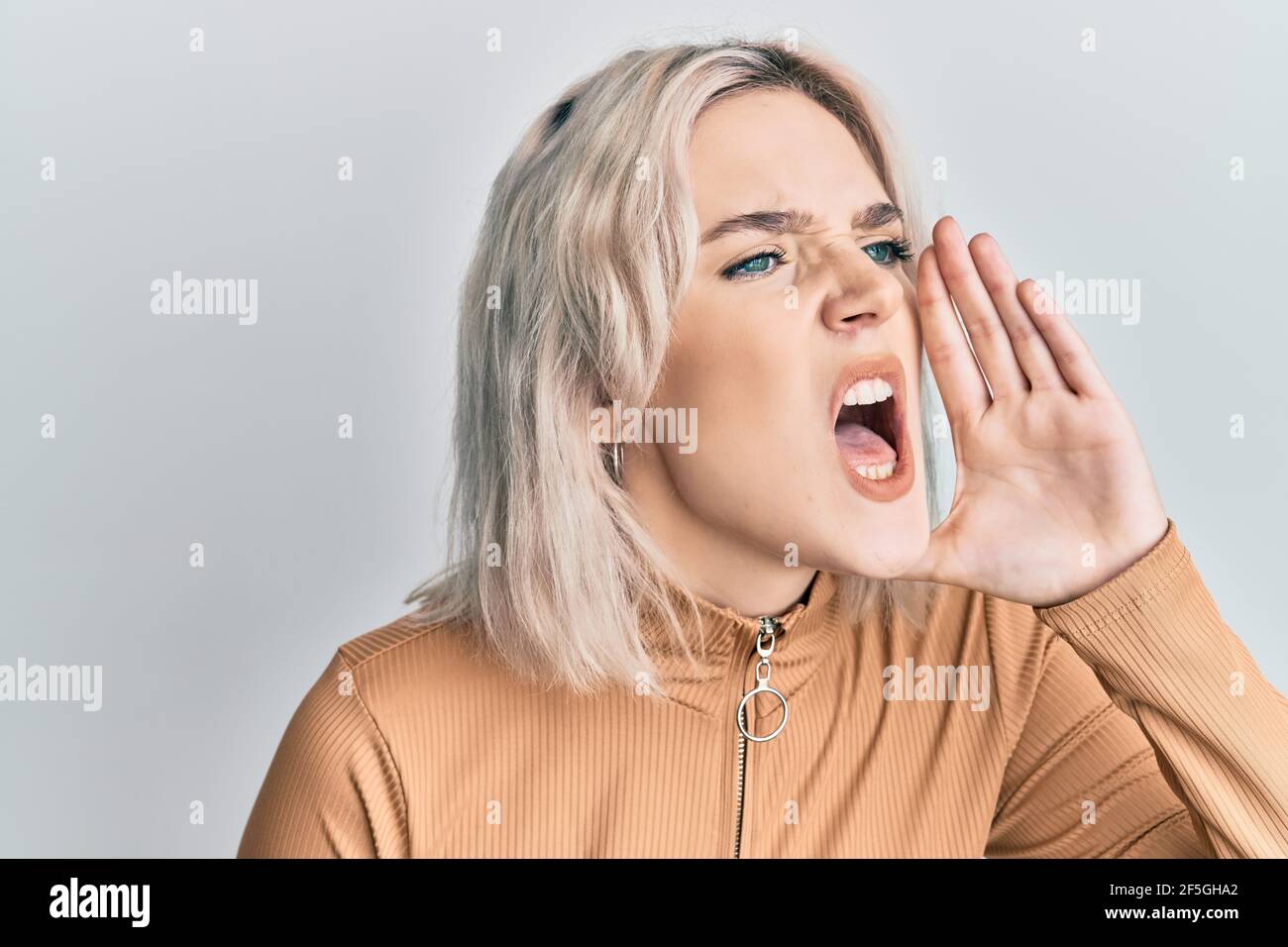 Young blonde girl wearing casual clothes shouting and screaming loud to ...