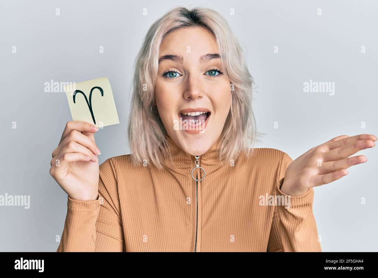 Young blonde girl holding paper with aries zodiac sign celebrating ...