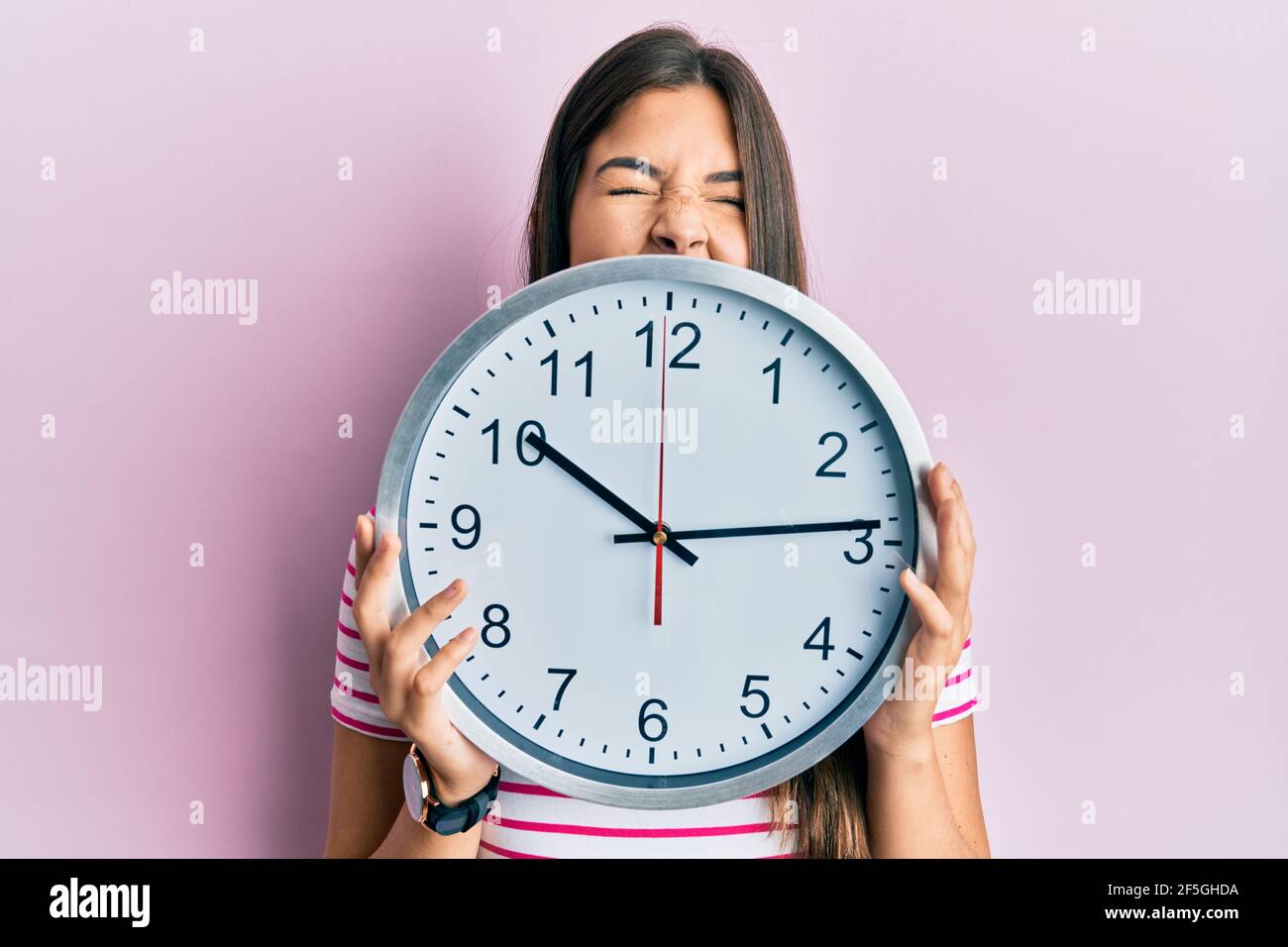 Young brunette woman holding big clock covering face angry and mad ...