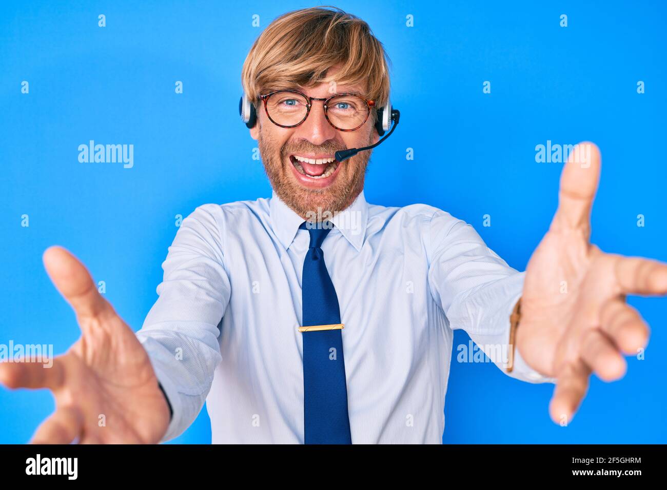Young blond man wearing call center agent headset looking at the camera ...