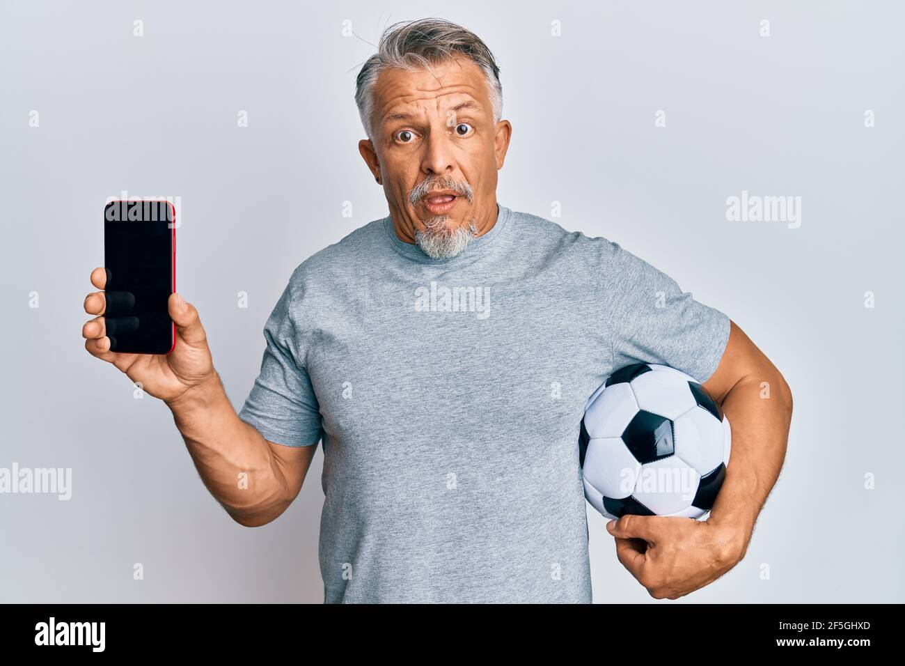 Middle age grey-haired man holding football ball showing smartphone ...