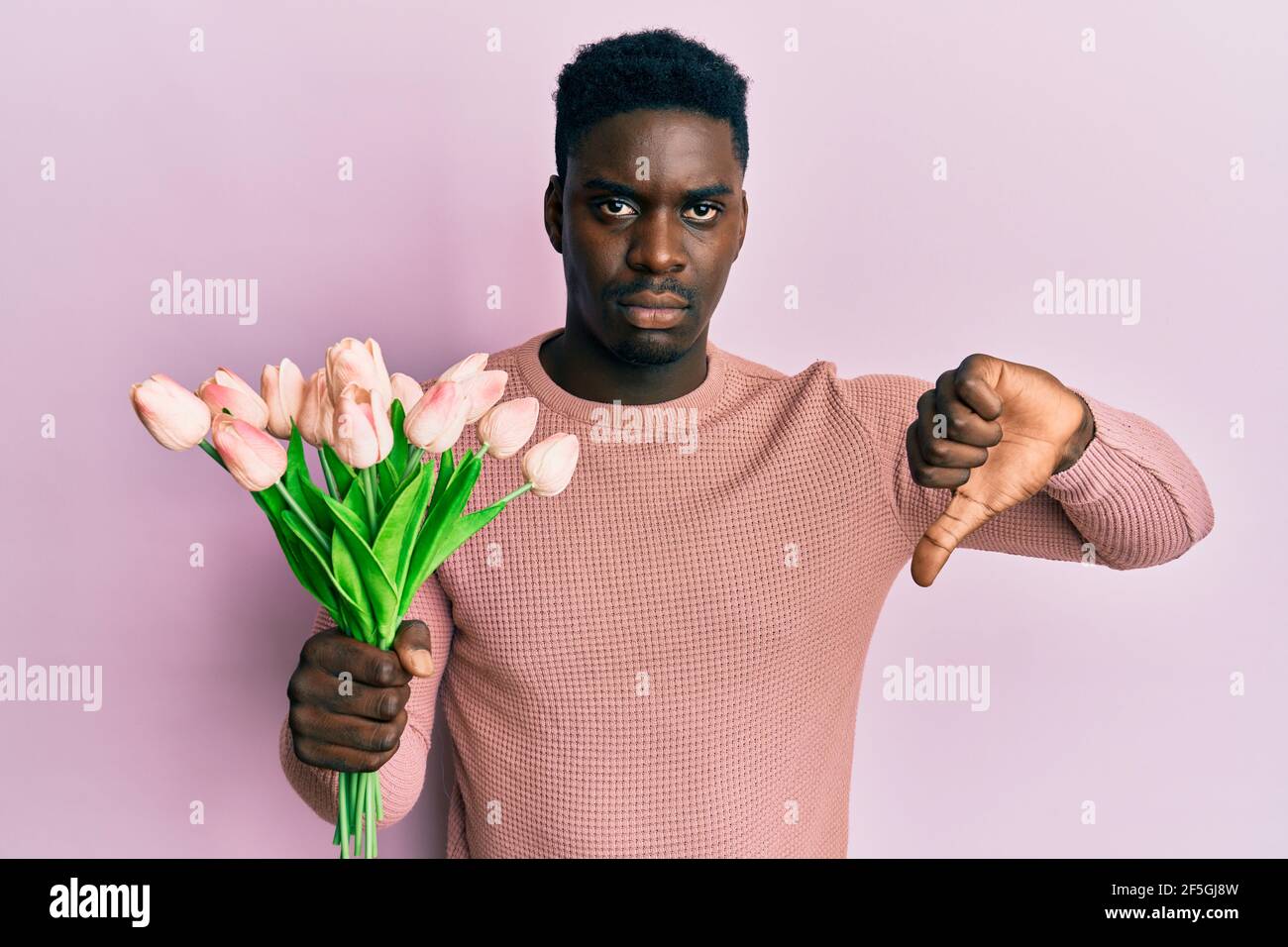 Handsome black man holding bouquet of pink tulips flowers with angry ...