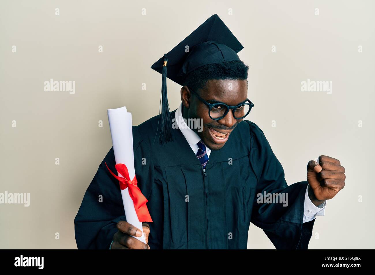 Handsome black man wearing graduation cap and ceremony robe holding ...