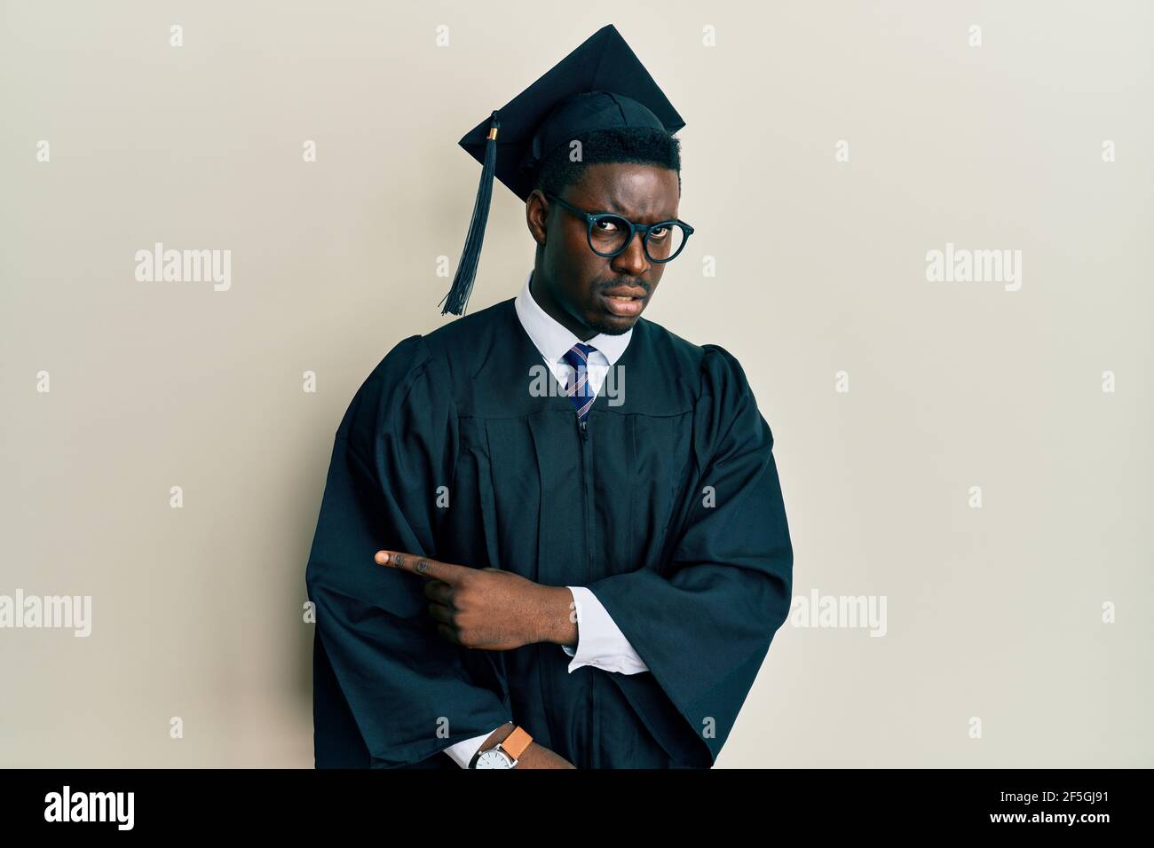 Handsome black man wearing graduation cap and ceremony robe pointing ...