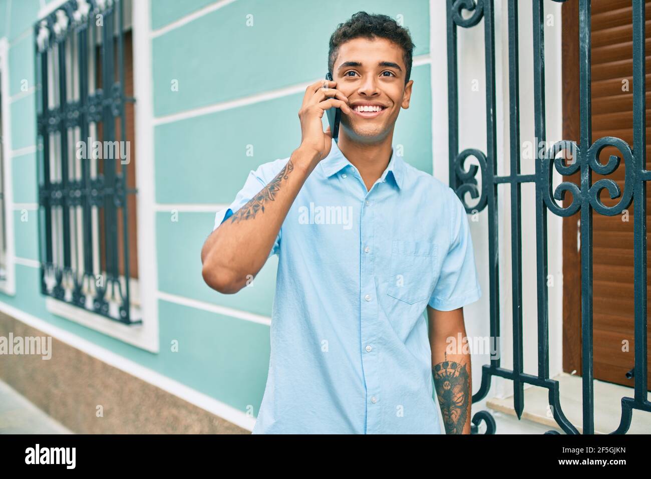 Young latin man smiling happy using smartphone walking at the city ...