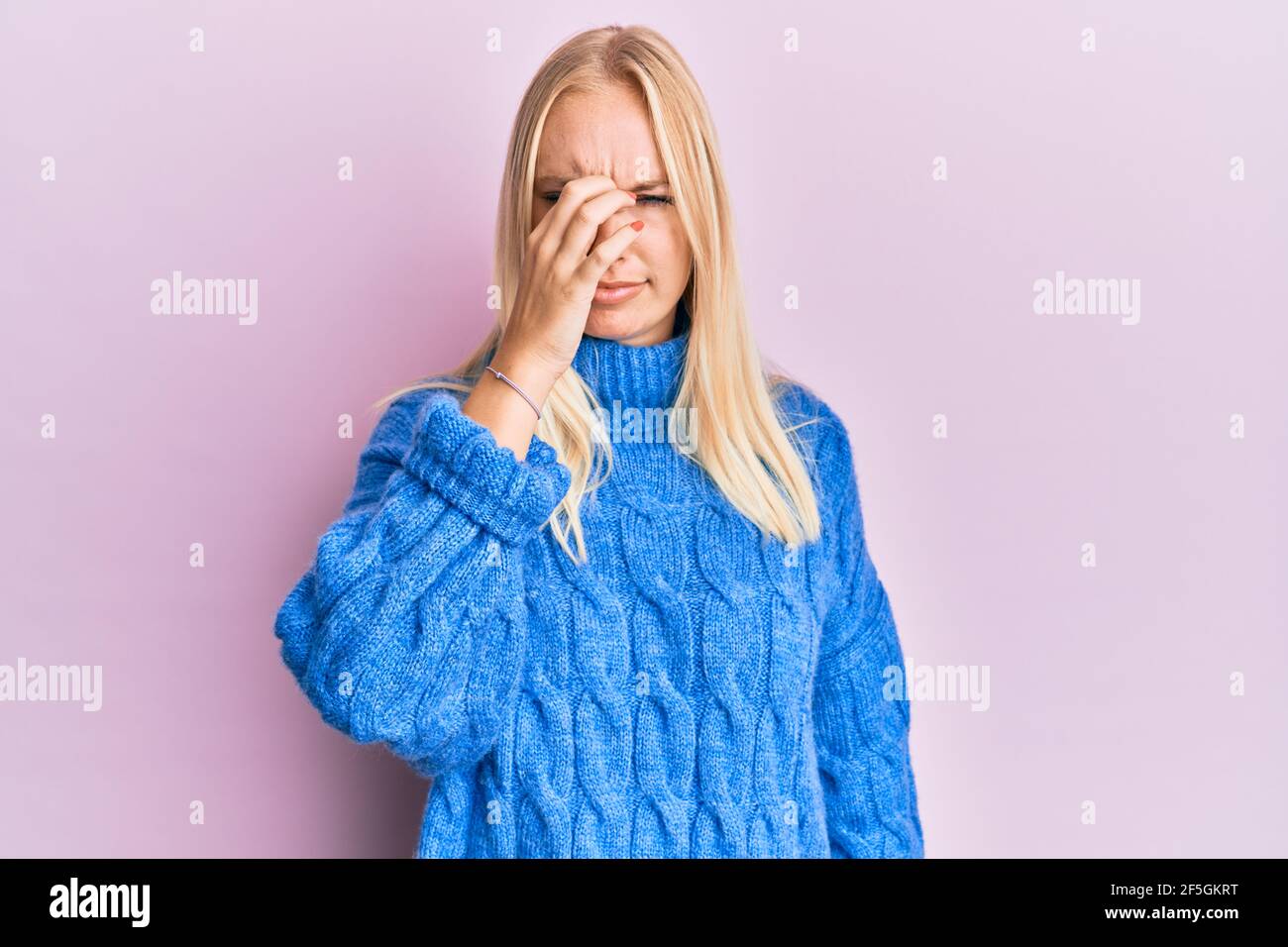 Young blonde girl wearing wool winter sweater tired rubbing nose and ...