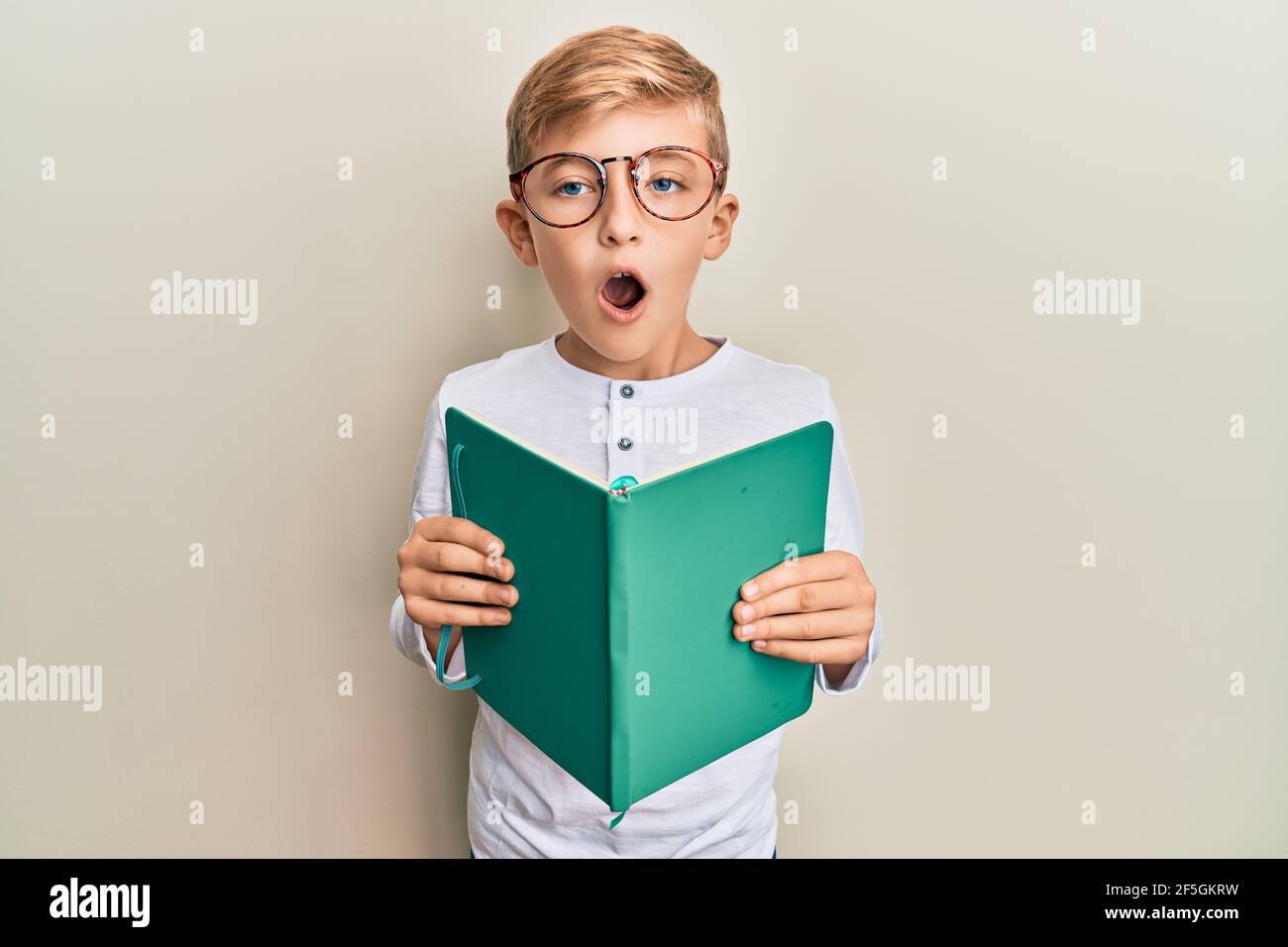 Little caucasian boy kid reading a book wearing glasses afraid and ...