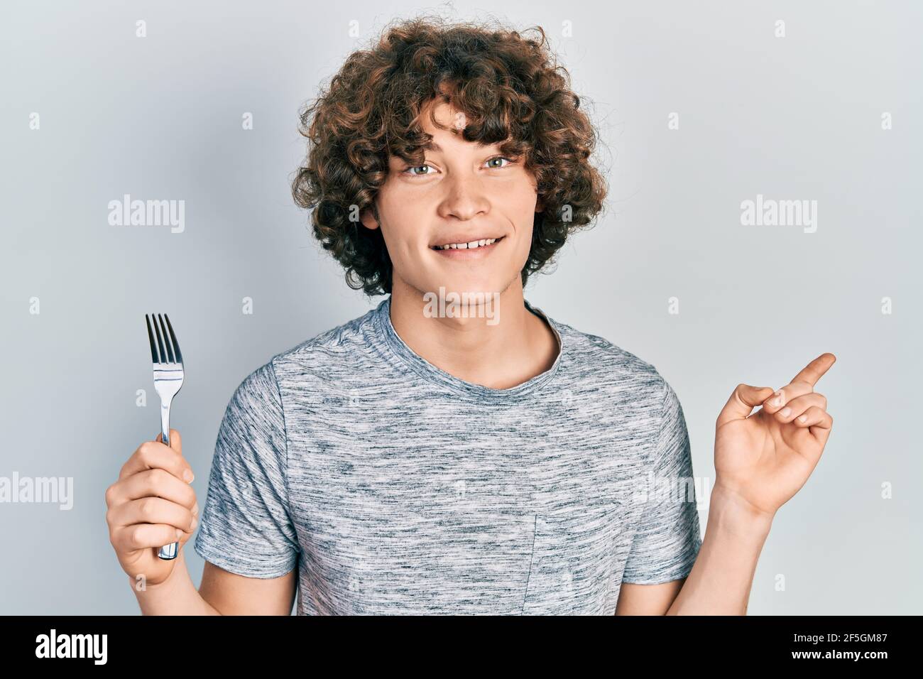 Handsome young man holding one silver fork smiling happy pointing with ...