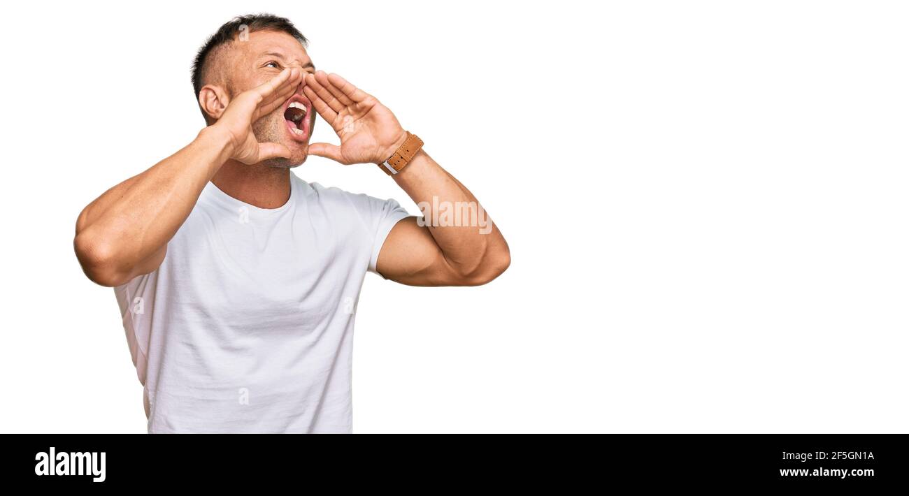 Handsome muscle man wearing casual white tshirt shouting angry out loud ...
