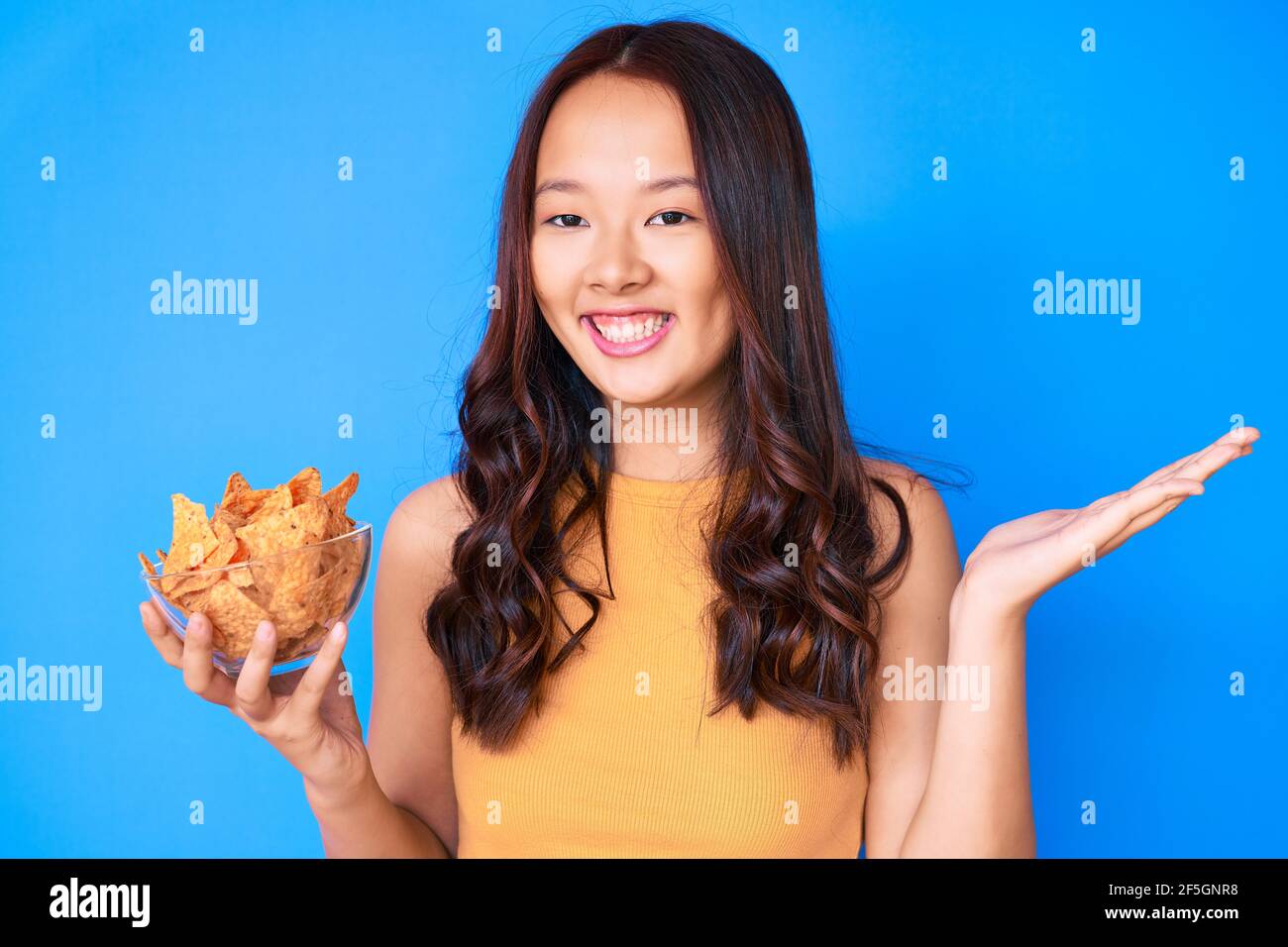 Young beautiful chinese girl holding nachos potato chips celebrating ...