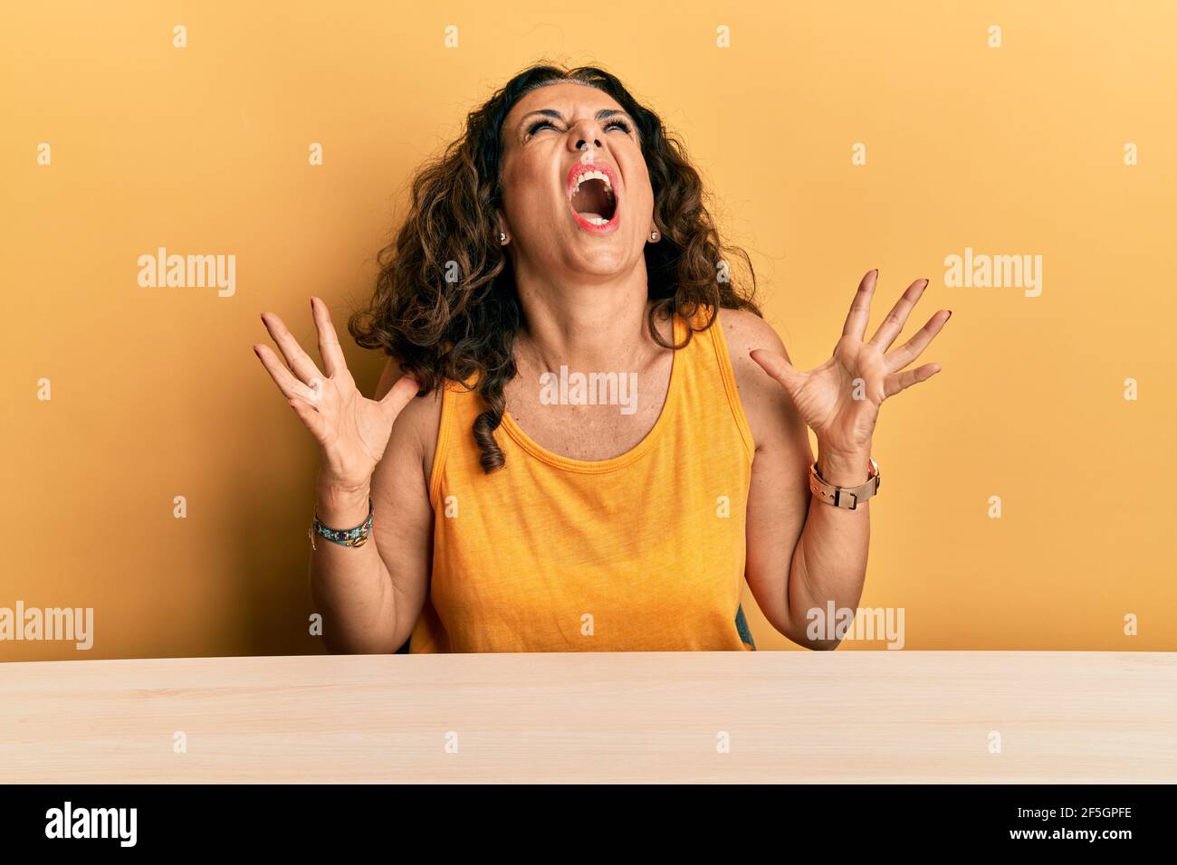 Beautiful middle age woman wearing casual clothes sitting on the table ...