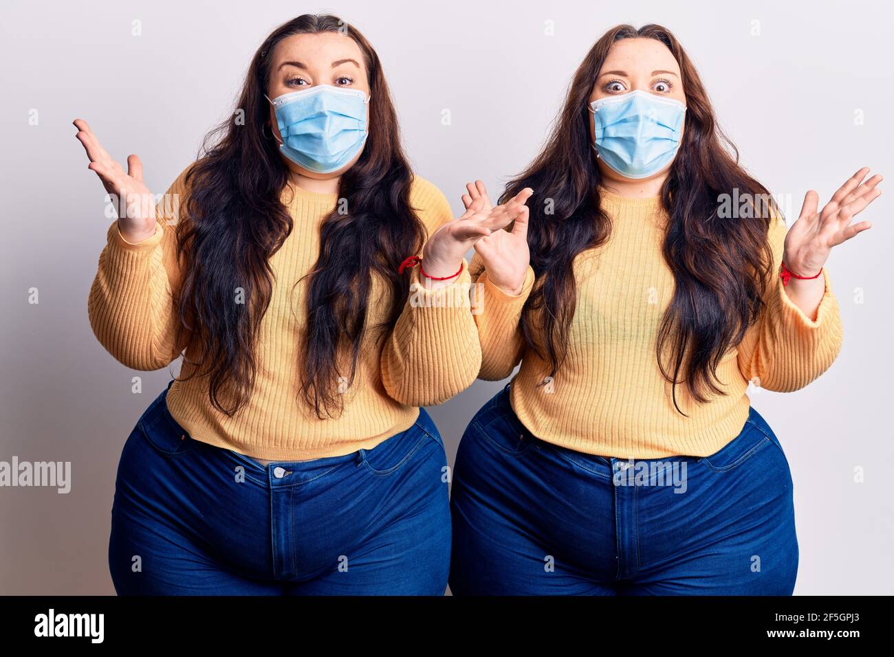 Young plus size twins wearing medical mask celebrating crazy and amazed ...