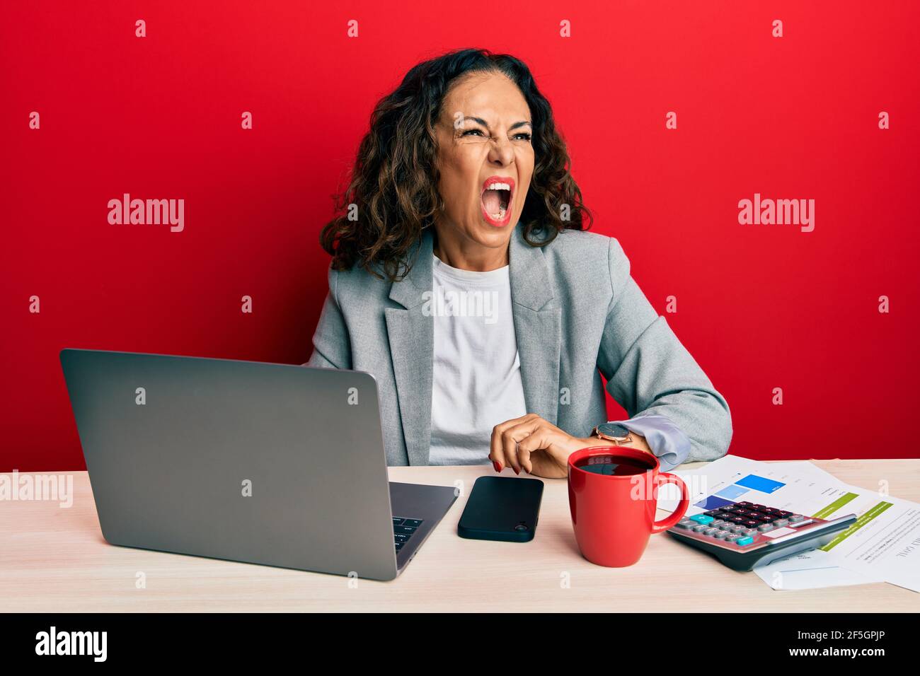 Beautiful middle age woman working at the office drinking a cup of ...