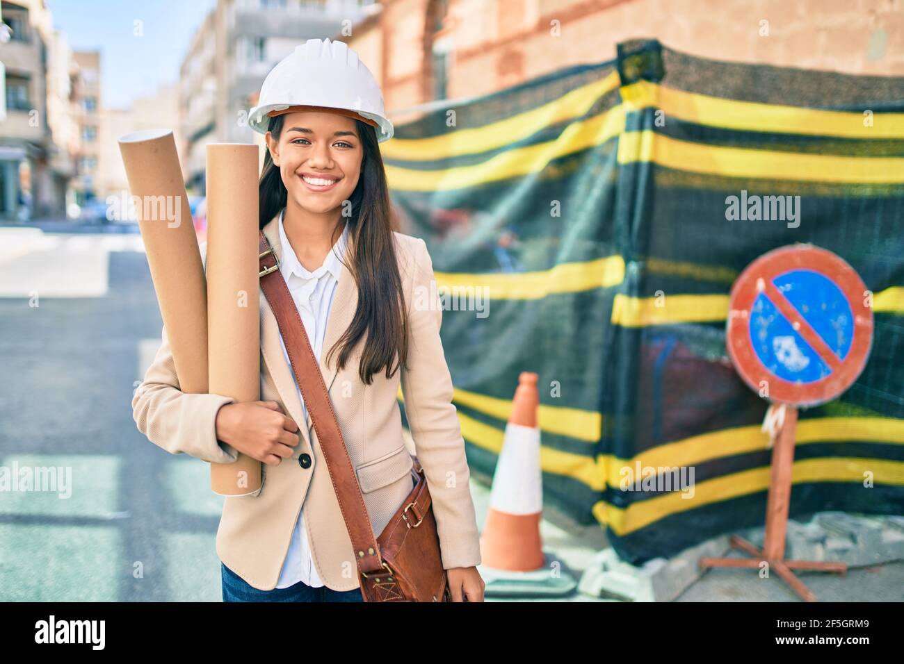 Young latin architect girl smiling happy holding blueprints standing at ...