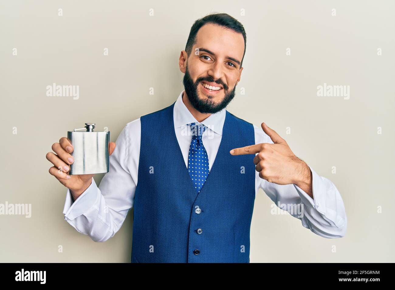 Young man with beard drinking whiskey from flask pointing finger to one ...