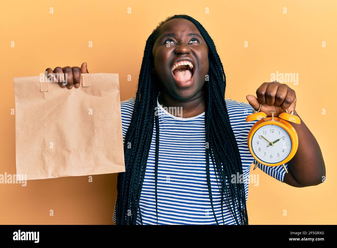 Young black woman with braids holding take away food and alarm clock ...