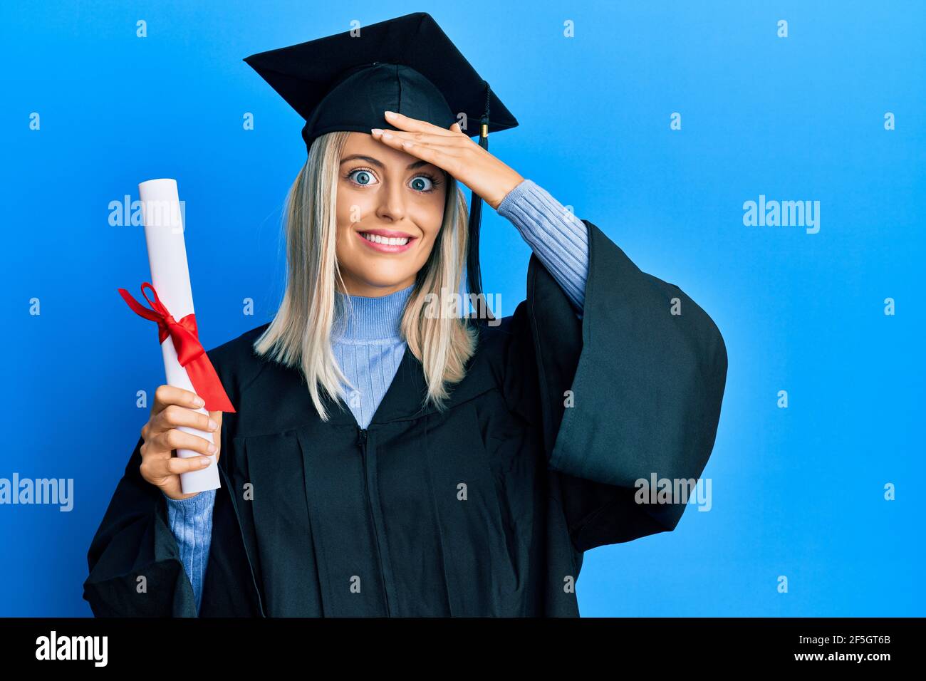 Beautiful blonde woman wearing graduation cap and ceremony robe holding ...
