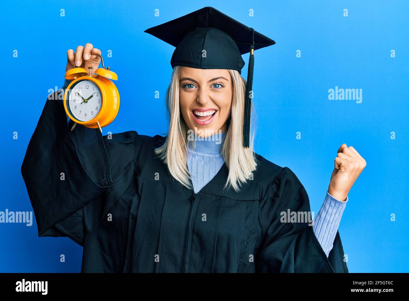 Beautiful blonde woman wearing graduation cap and ceremony robe holding ...
