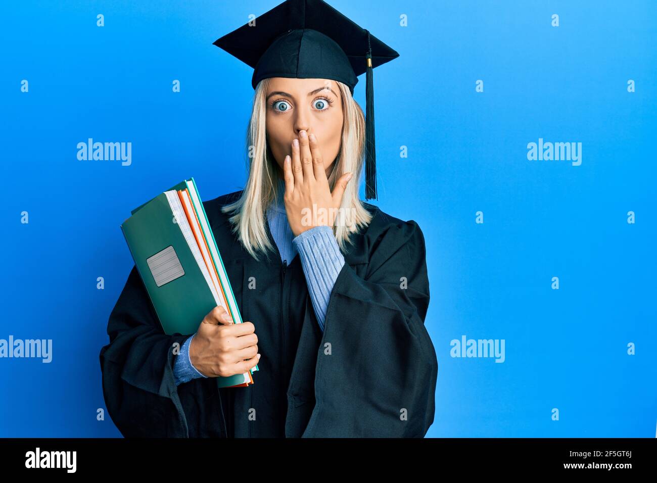Beautiful blonde woman wearing graduation cap and ceremony robe holding ...