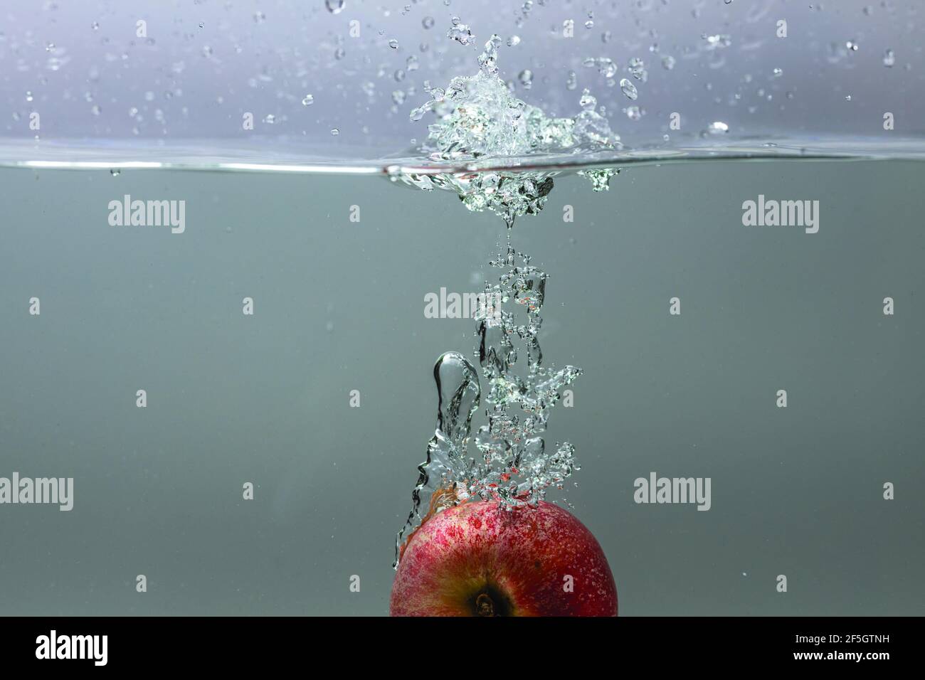 Close up view of colorful apple falling in water on grey background ...