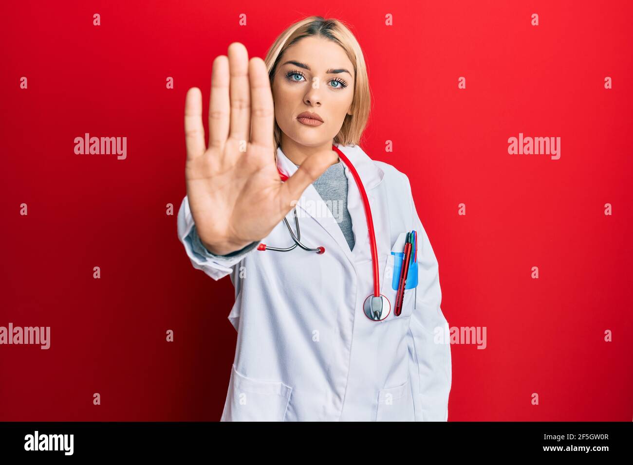 Young caucasian woman wearing doctor uniform and stethoscope doing stop ...