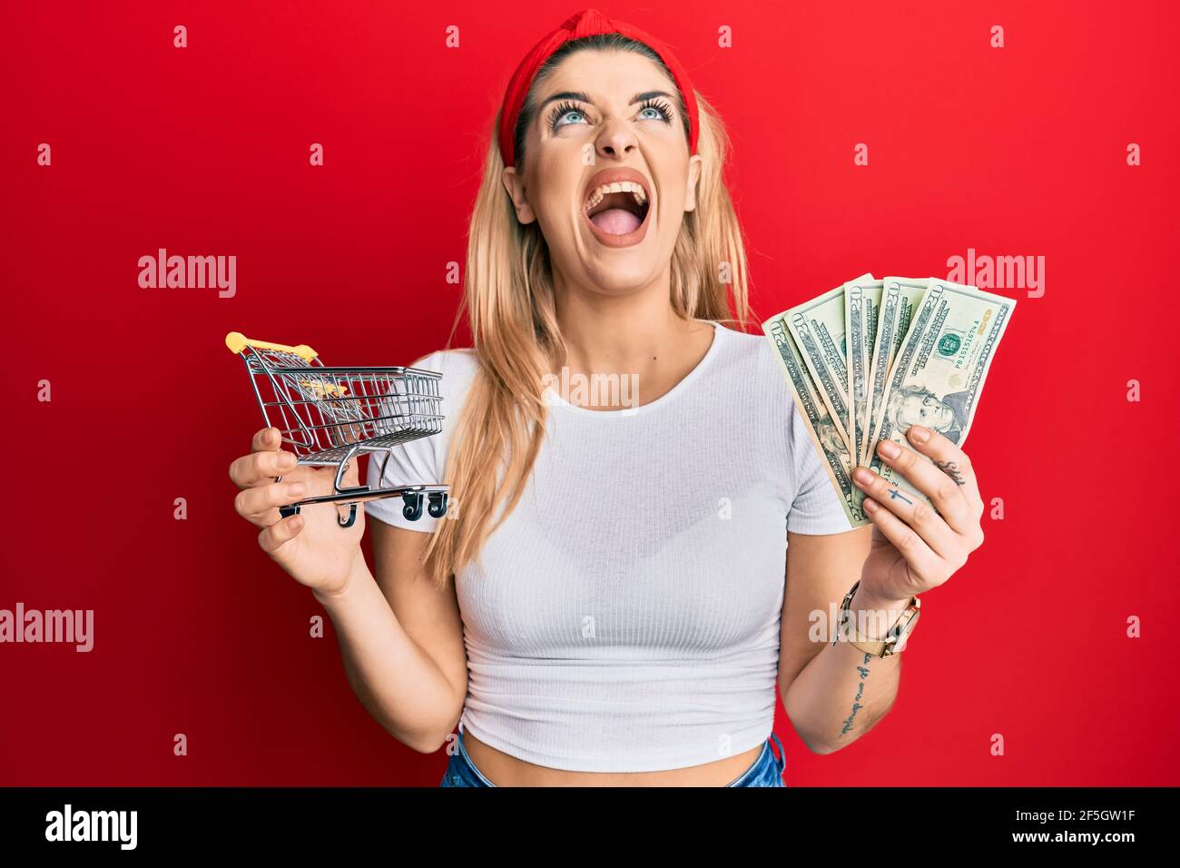 Young caucasian woman holding small supermarket shopping cart and ...