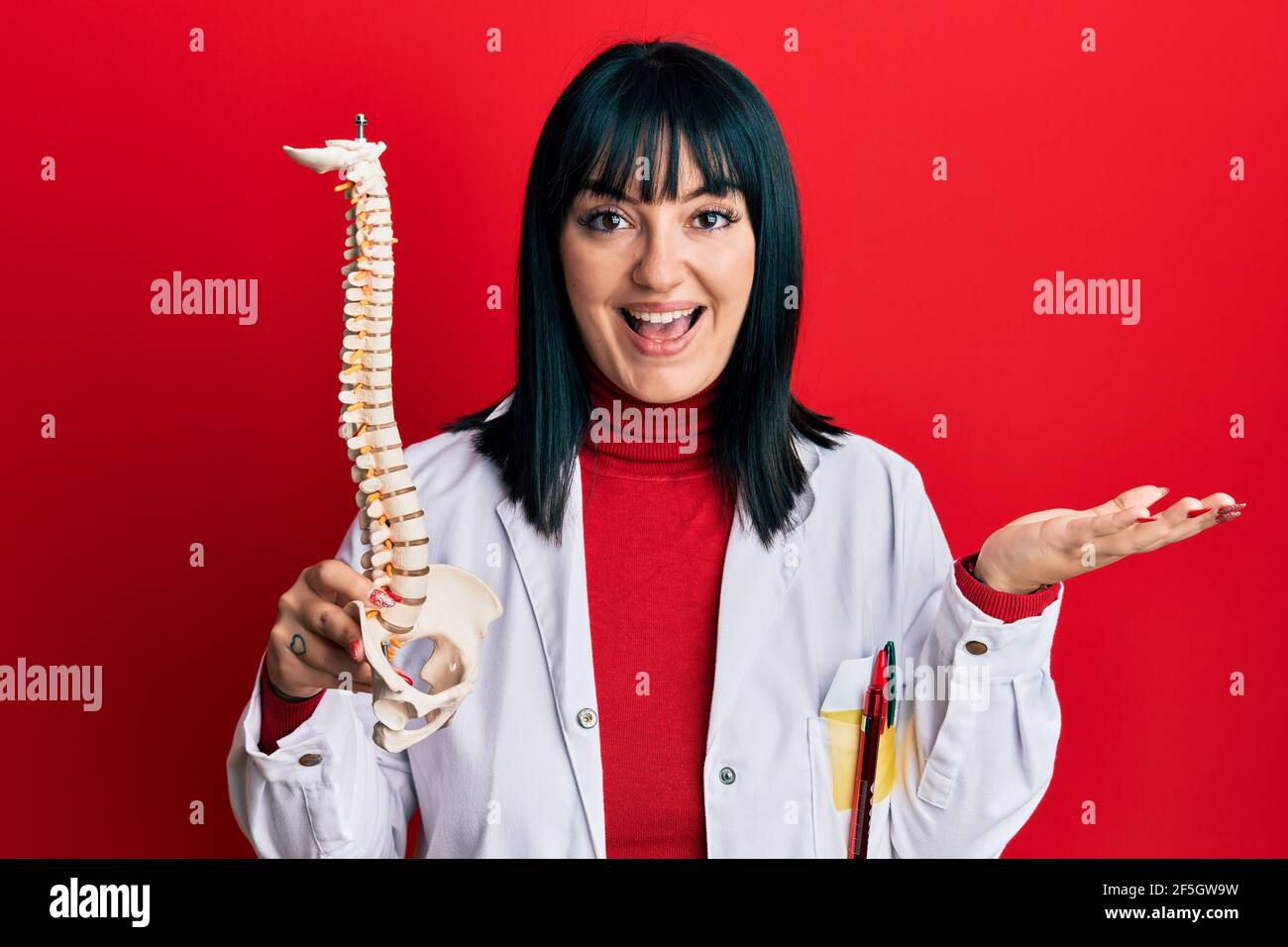 Young hispanic doctor woman holding anatomical model of spinal column ...
