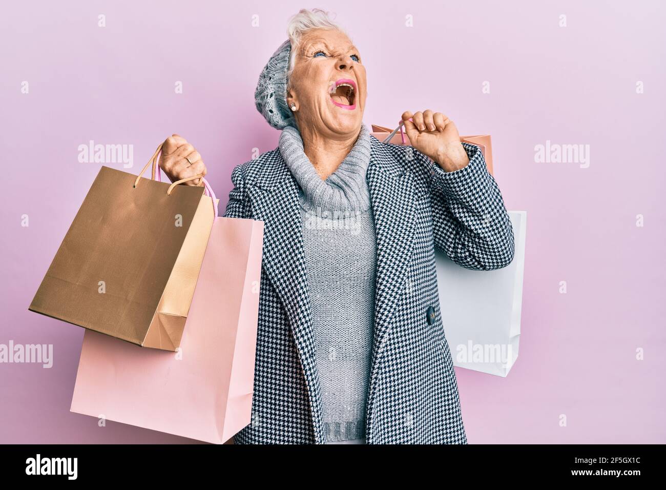 Senior grey-haired woman holding shopping bags angry and mad screaming ...