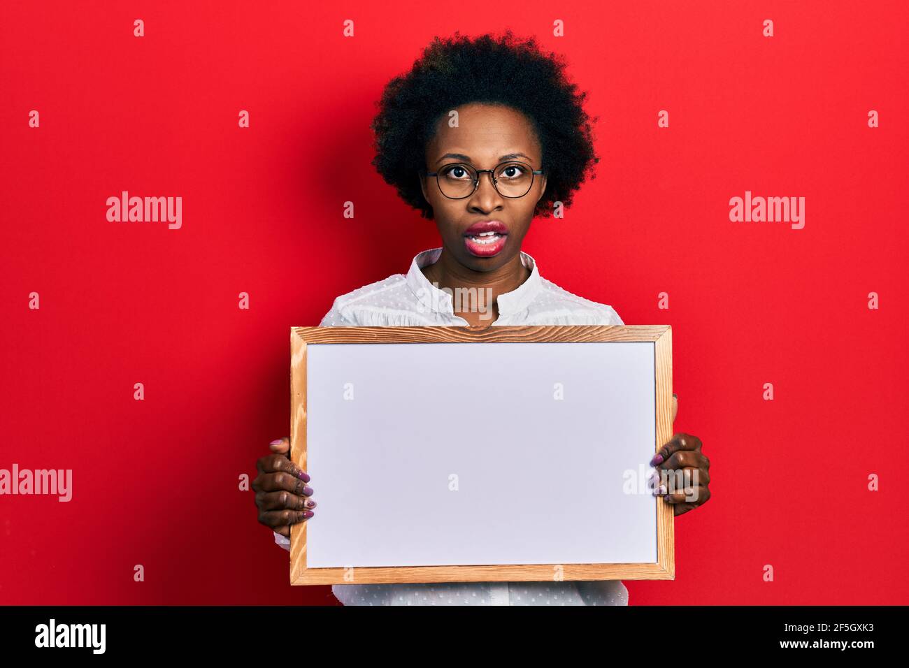 Young african american woman holding empty white chalkboard in shock ...